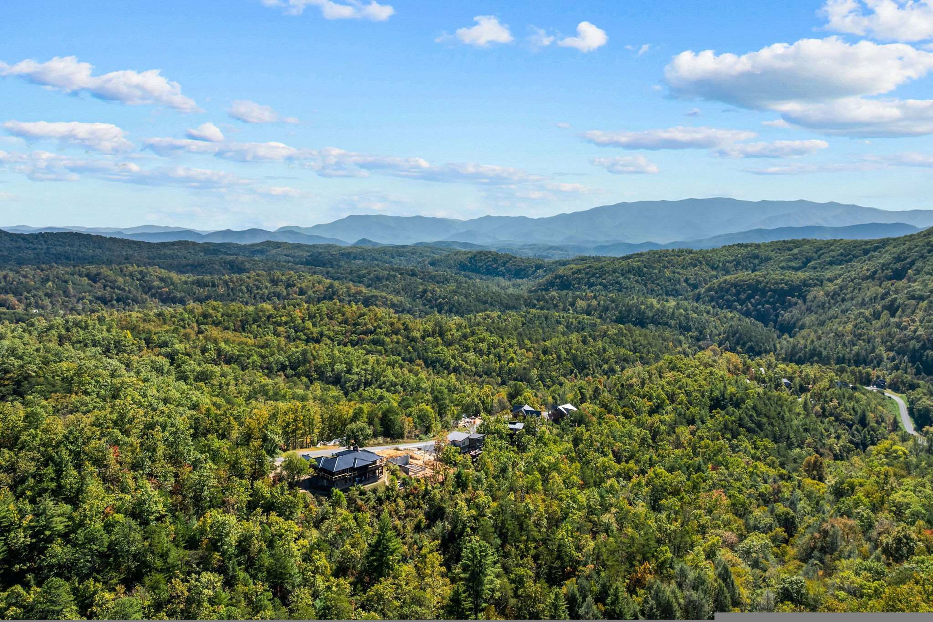 Uma área arborizada com vários edifícios, provavelmente um resort ou pousada, cercada por montanhas e um céu claro.