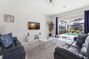 Uma sala de estar moderna com televisão, sofá, mesa de centro e vista para uma piscina.