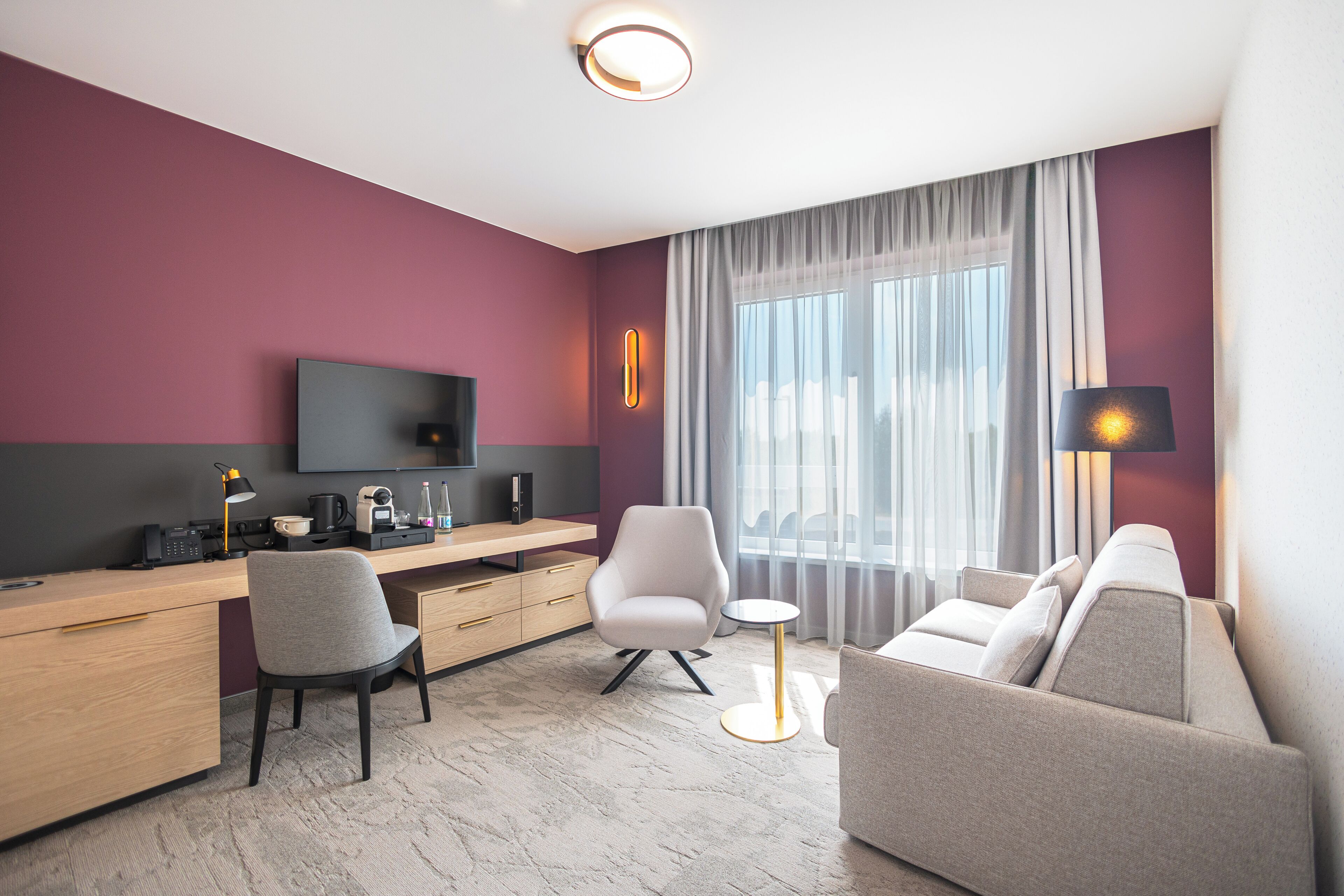 Quarto de hotel moderno com uma mesa, televisão, sofá e luminária.