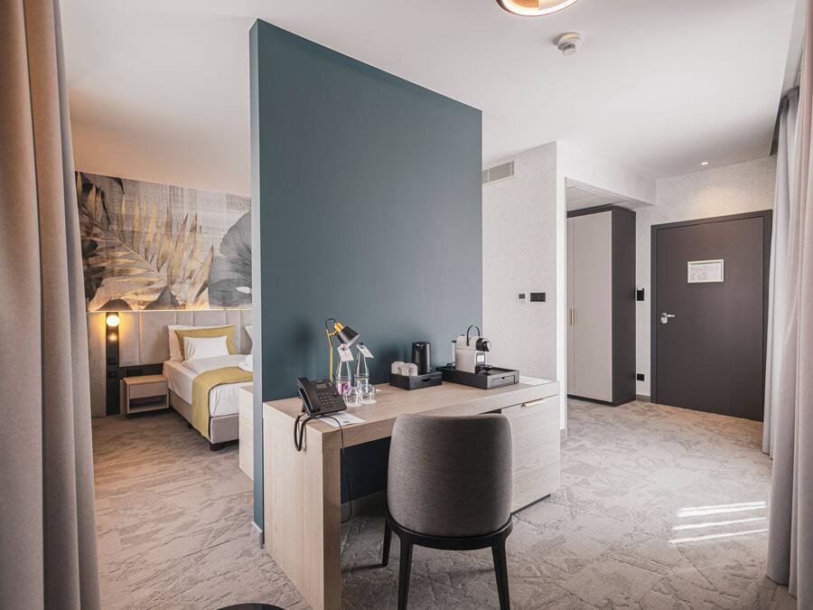 Quarto de hotel moderno com escrivaninha, cadeira, cama e obra de arte na parede.