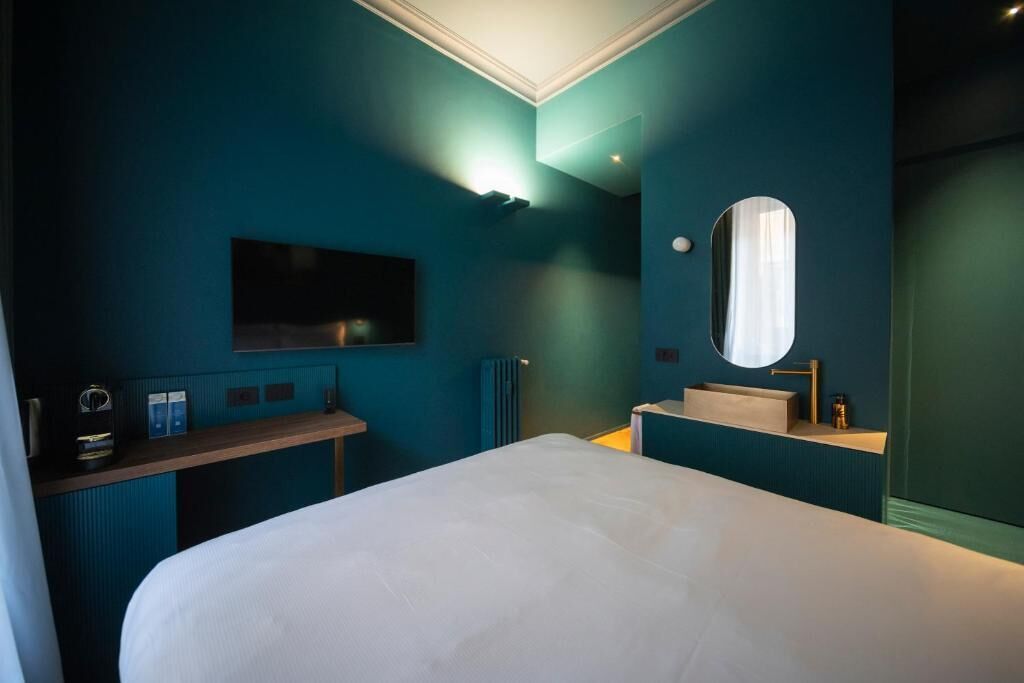 Quarto de hotel moderno com uma cama grande, uma mesa de cabeceira, um espelho e uma pia embutida.