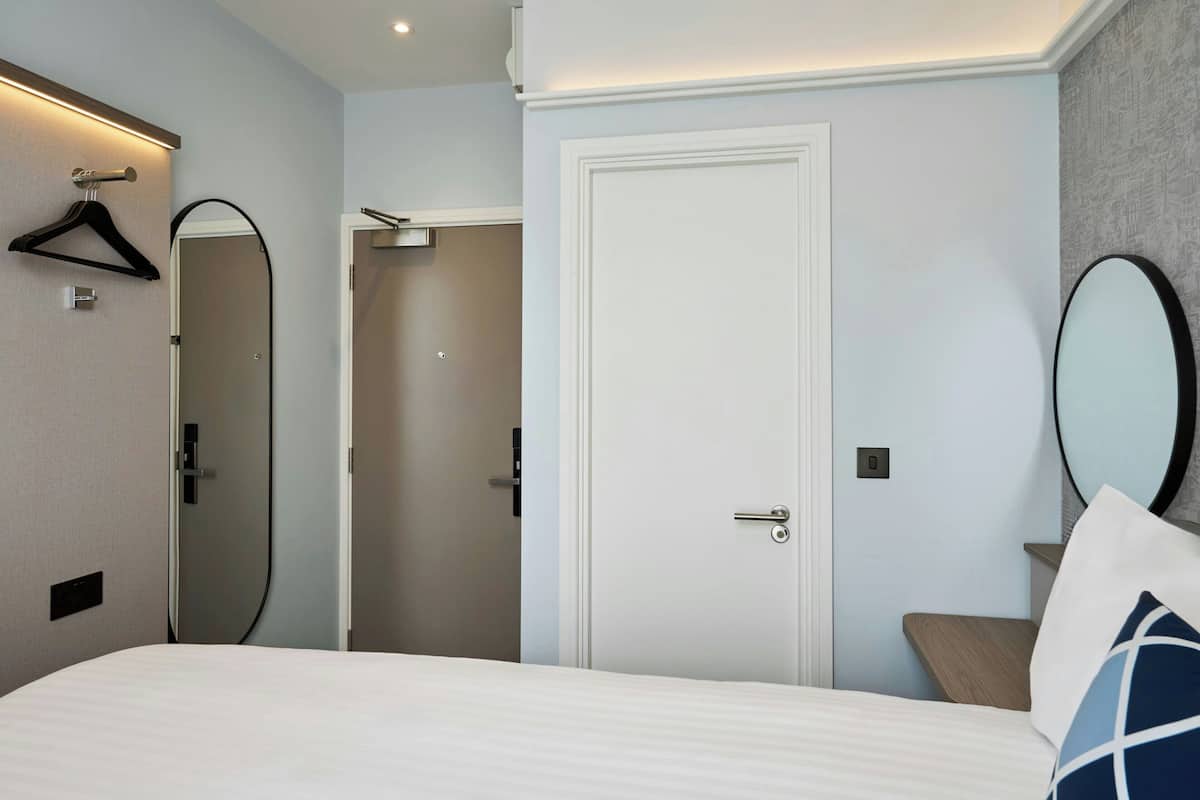Quarto de hotel com cama, porta, espelho e cabideiro.