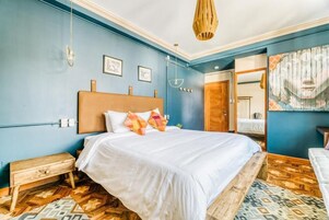 Quarto com cama, mesas de cabeceira de madeira, piso estampado e luminária pendente.
