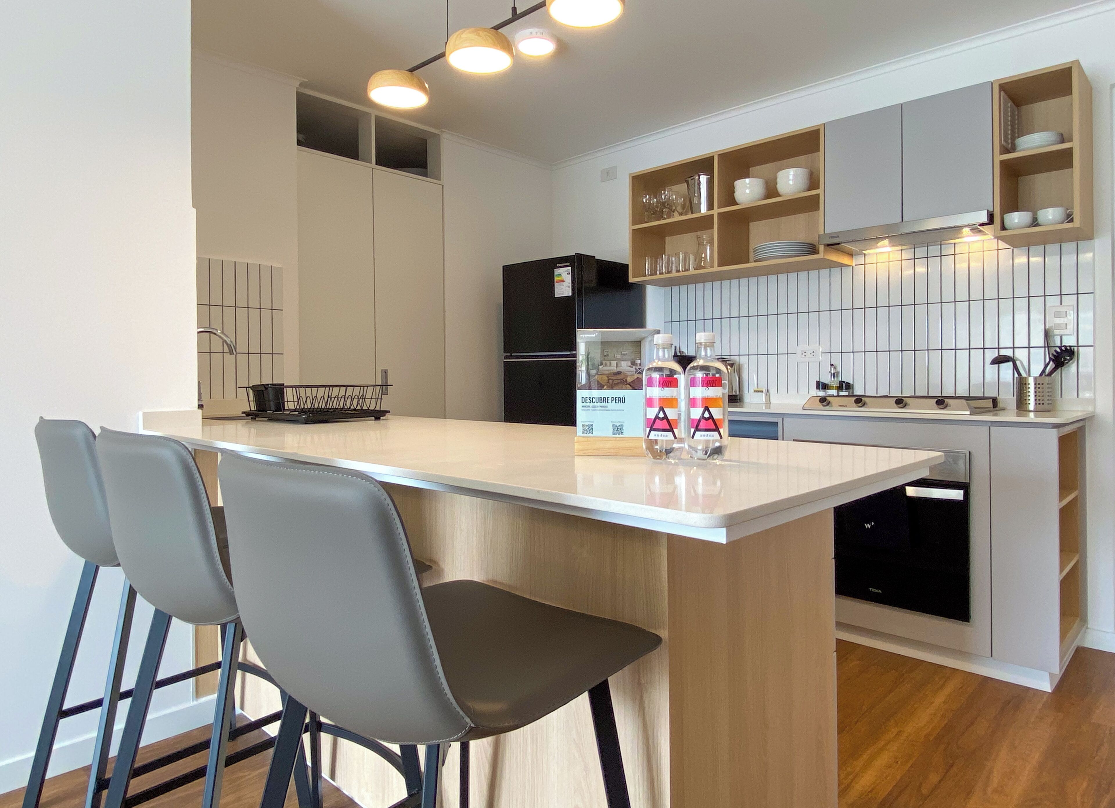 Cozinha moderna com ilha central, banquetas, frigorífico e forno embutido.
