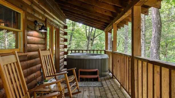 Uma cabana de madeira com hidromassagem no alpendre, rodeada por árvores.