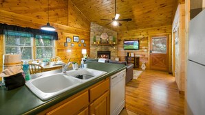 Interior acolhedor de uma cabana, com decoração em madeira, cozinha equipada com pia e lava-louças, lareira e televisão.