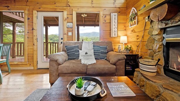 Interior de uma cabana de madeira com sofá, lareira e uma placa de boas-vindas.