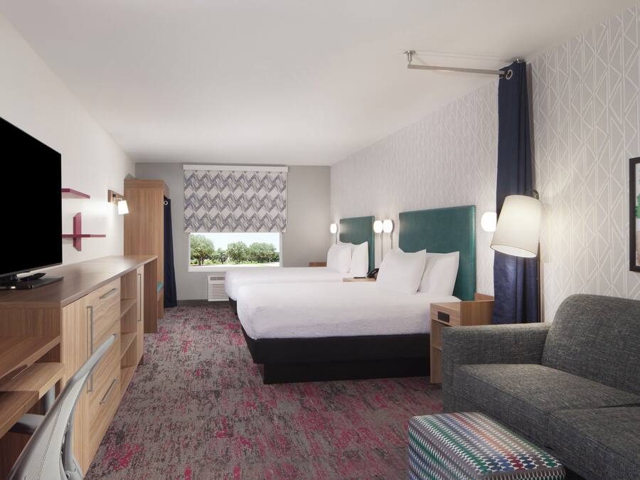Quarto de hotel com cama, televisão, escrivaninha e sofá.
