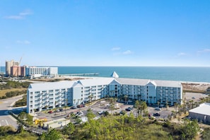 Um hotel grande com vários andares e estacionamento, situado perto de uma praia e do oceano.