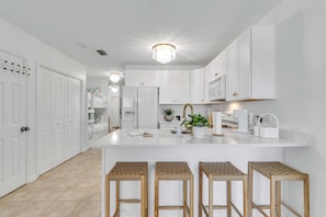 Cozinha moderna com armários brancos, uma ilha central com banquetas e um lustre.