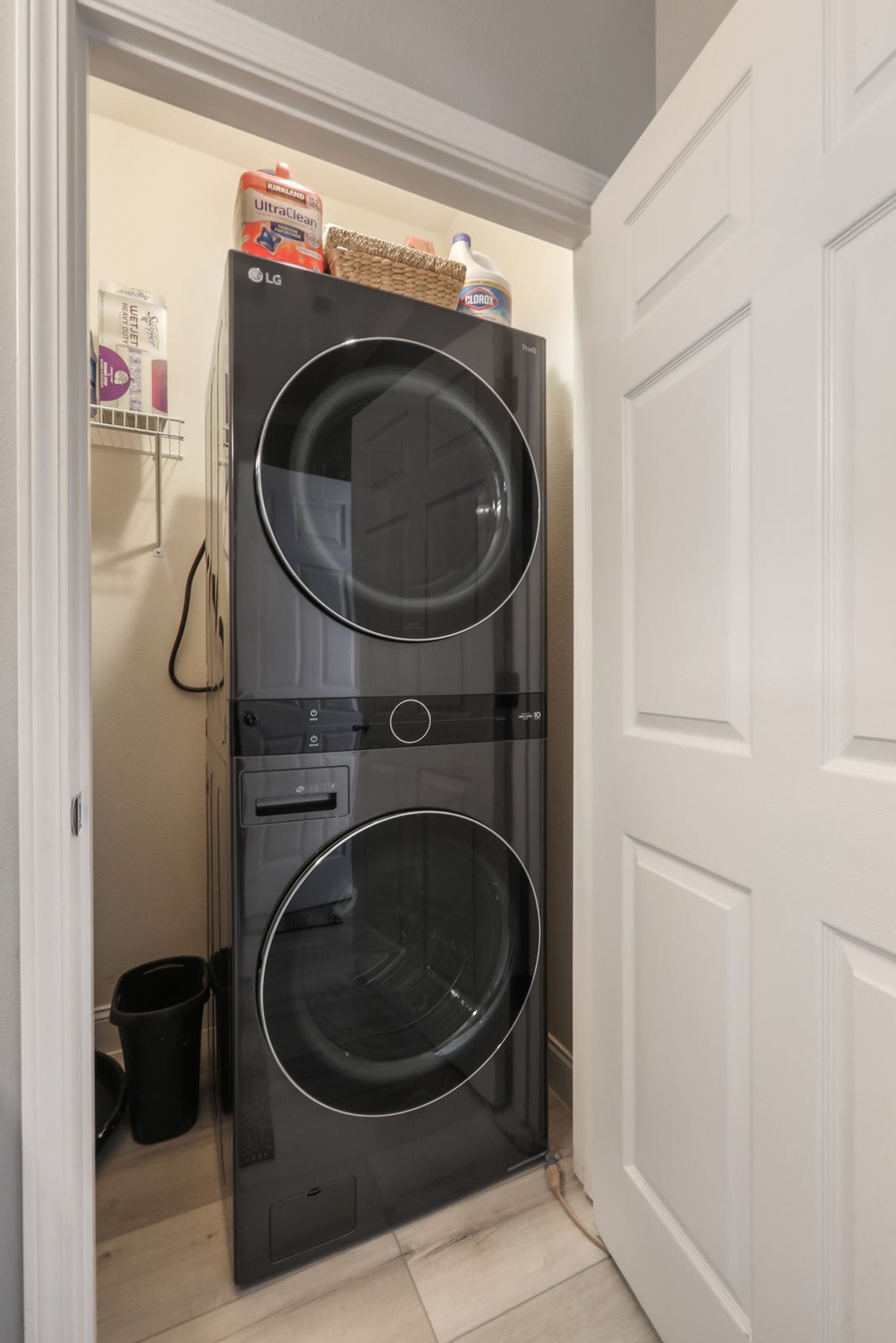 Lavanderia compacta e moderna com máquina de lavar e secar lado a lado, um cesto no topo e produtos de lavagem na parede.