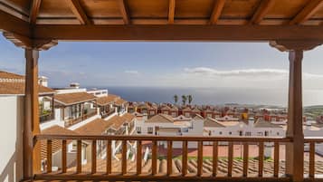 Varanda com guarda-corpo de madeira, vista para uma cidade costeira com edifícios de telhado em terracota e do mar.