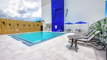 Piscina com borda azul, espreguiçadeiras e guarda-sóis.
