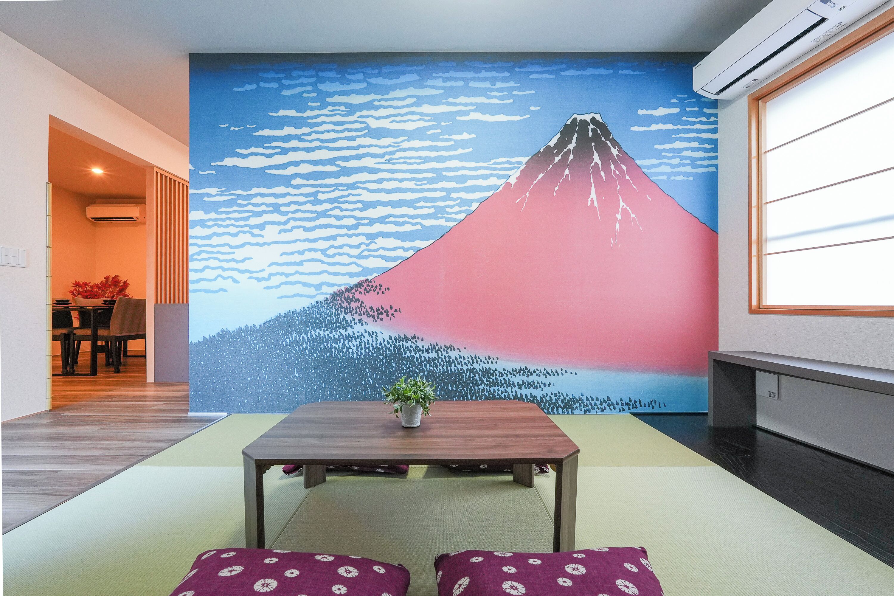 Um espaço com esteiras de tatame, uma mesinha baixa, almofadas e um mural na parede com o desenho de uma montanha.