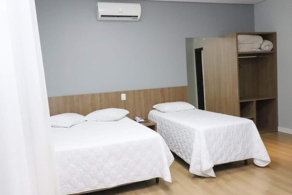 Quarto com duas camas, um guarda-roupa de madeira e um aparelho de ar condicionado.