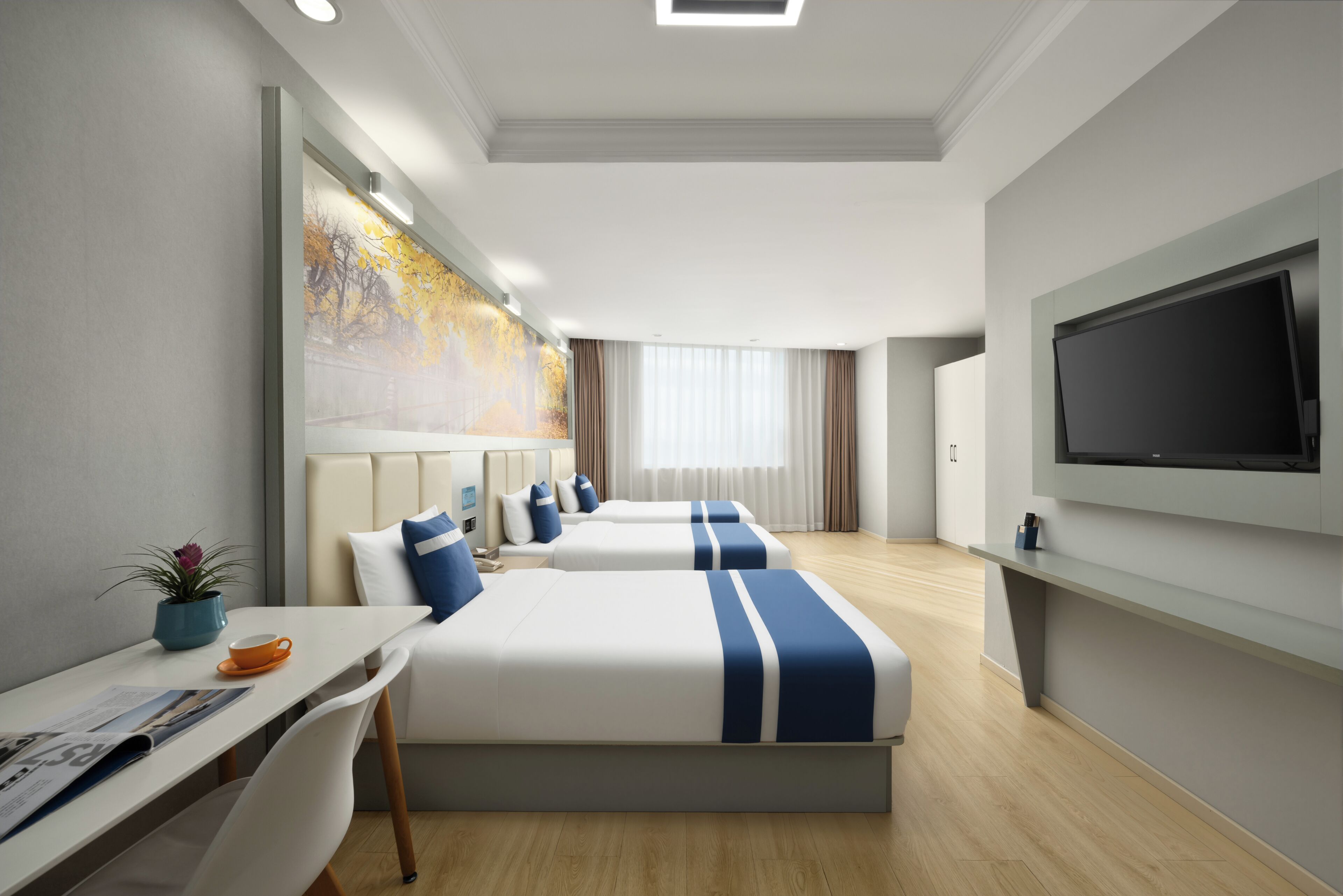 Quarto de hotel com cama, escrivaninha com cadeira, televisão e uma pintura grande na parede.