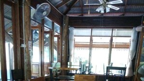 Uma mesa de jantar de madeira com cadeiras, um ventilador de teto e grandes janelas.
