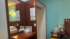 Quarto de hotel com toucador de madeira, espelho, um pequeno banquinho, minibar amarelo e chaleira.