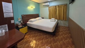 Quarto de hotel com cama, escrivaninha, mesa de cabeceira, ar condicionado e janela com cortinas.