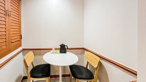 Um quarto pequeno com uma mesa branca e duas cadeiras, uma chaleira e um tabuleiro com uma chávena e um prato pequeno.