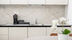 Cozinha moderna com backsplash de mármore, máquina de café embutida e pia de aço inoxidável.