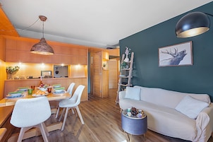 Uma sala de estar moderna com um sofá branco, uma área de jantar com mesa e cadeiras de madeira, e uma cozinha ao fundo.