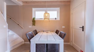Uma sala de jantar com uma mesa de madeira, seis cadeiras, um lustre e uma janela, além de uma porta.