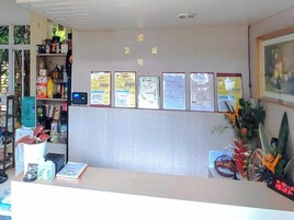 Um balcão de atendimento com um visor digital, quadros de certificados na parede e diversos objetos nas prateleiras.