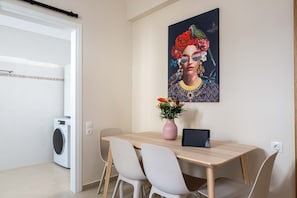 Uma área de refeições com uma mesa, cadeiras, um vaso com flores, um tablet e uma máquina de lavar ao fundo.