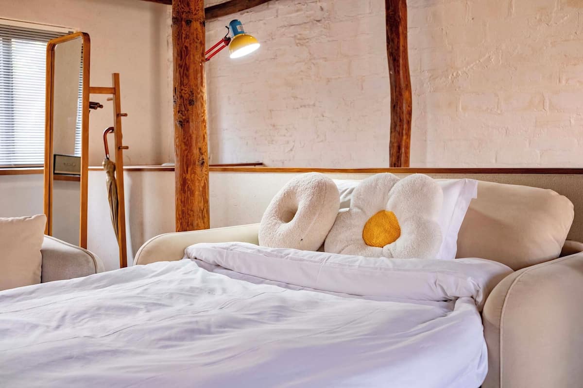 Uma cama bem arrumada com roupa de cama branca, uma escada de madeira encostada na parede e um abajur amarelo.