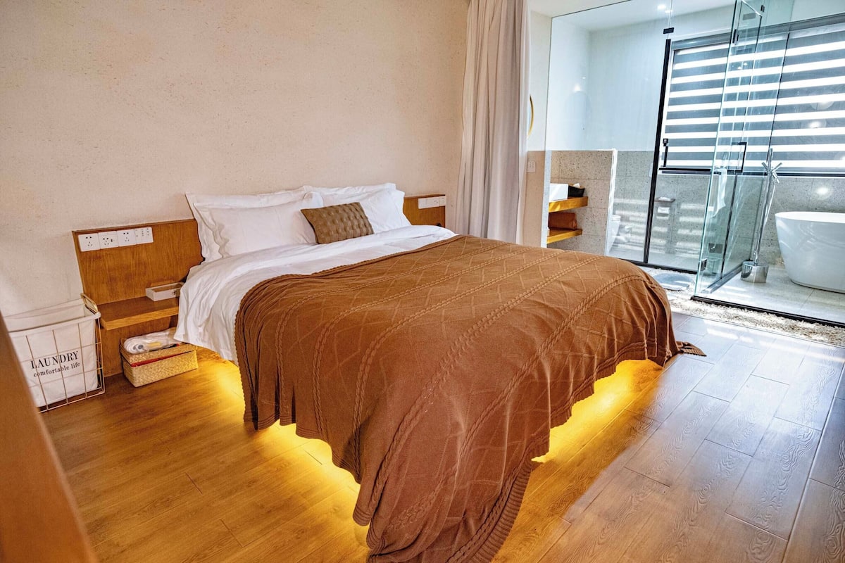 Quarto de hotel moderno com cama de madeira, chuveiro de vidro e vista para a cidade.