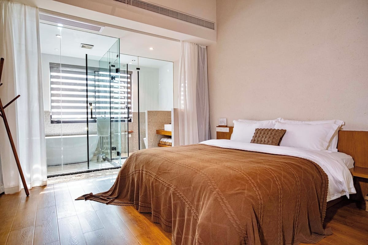 Quarto com uma cama grande, uma porta de vidro que dá para uma varanda e piso de madeira.