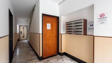 Um corredor com porta de madeira, um mural de avisos e piso de azulejos.