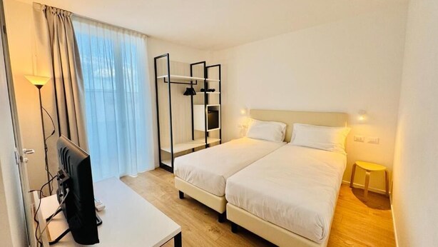 Quarto de hotel com duas camas, televisão, escrivaninha e janela com cortinas.