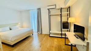 Quarto de hotel com cama, secretária com computador, televisão e guarda-roupa.