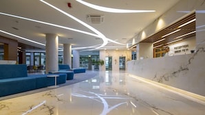 Um hall moderno com piso de mármore, áreas de estar em azul e um balcão de recepção.