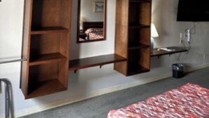 Quarto de hotel com cama, guarda-roupa de madeira, espelho, televisão e uma pequena mesa com abajur.