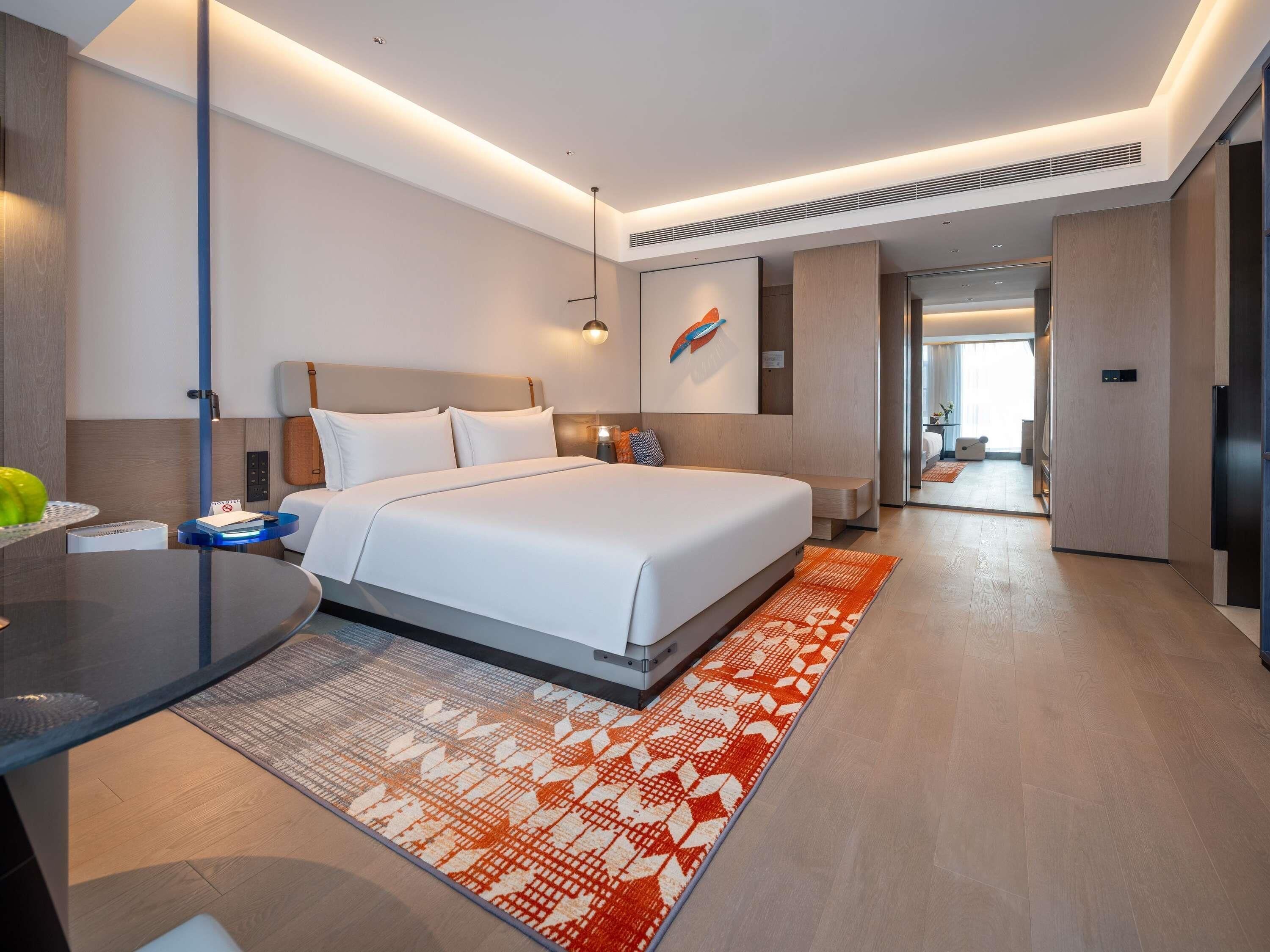 Quarto de hotel moderno com uma cama grande, uma escrivaninha e vista para o corredor.