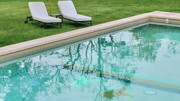 Piscina com duas espreguiçadeiras e um guarda-sol.
