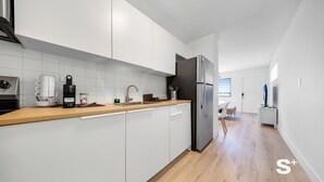 Cozinha moderna com armários brancos, geladeira de aço inoxidável e bancada de madeira.