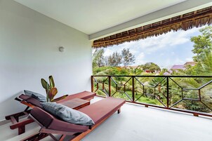 Varanda com guarda-corpo geométrico, um banco de madeira e vista para um jardim exuberante.