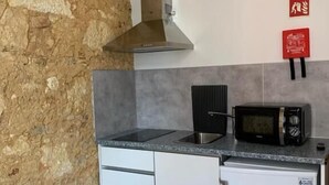 Uma cozinha compacta com parede de pedra, coifa de aço inoxidável, micro-ondas e uma geladeira pequena.