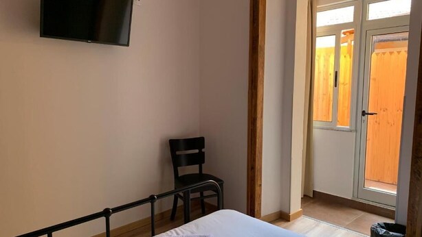 Quarto com cama, cadeira, televisão na parede e janela com vista para uma cerca de madeira.