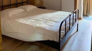 Quarto com parede de pedra, prateleira de madeira, estrutura de cama em metal e piso de madeira.