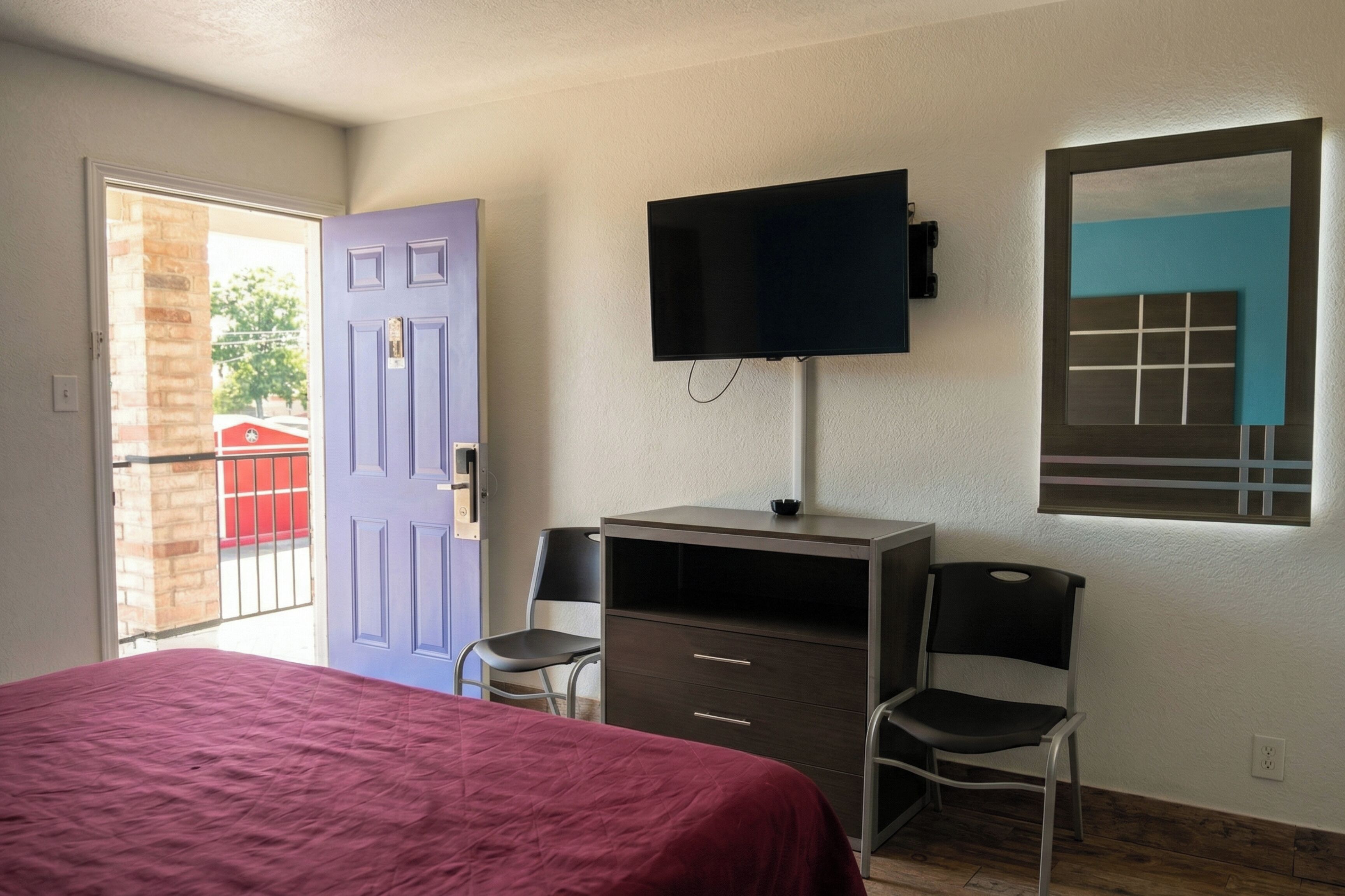 Quarto com cama, escrivaninha, cadeira, televisão e porta.