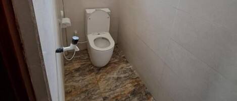 Uma casa de banho pequena com sanita, chuveiro e chão em mármore.