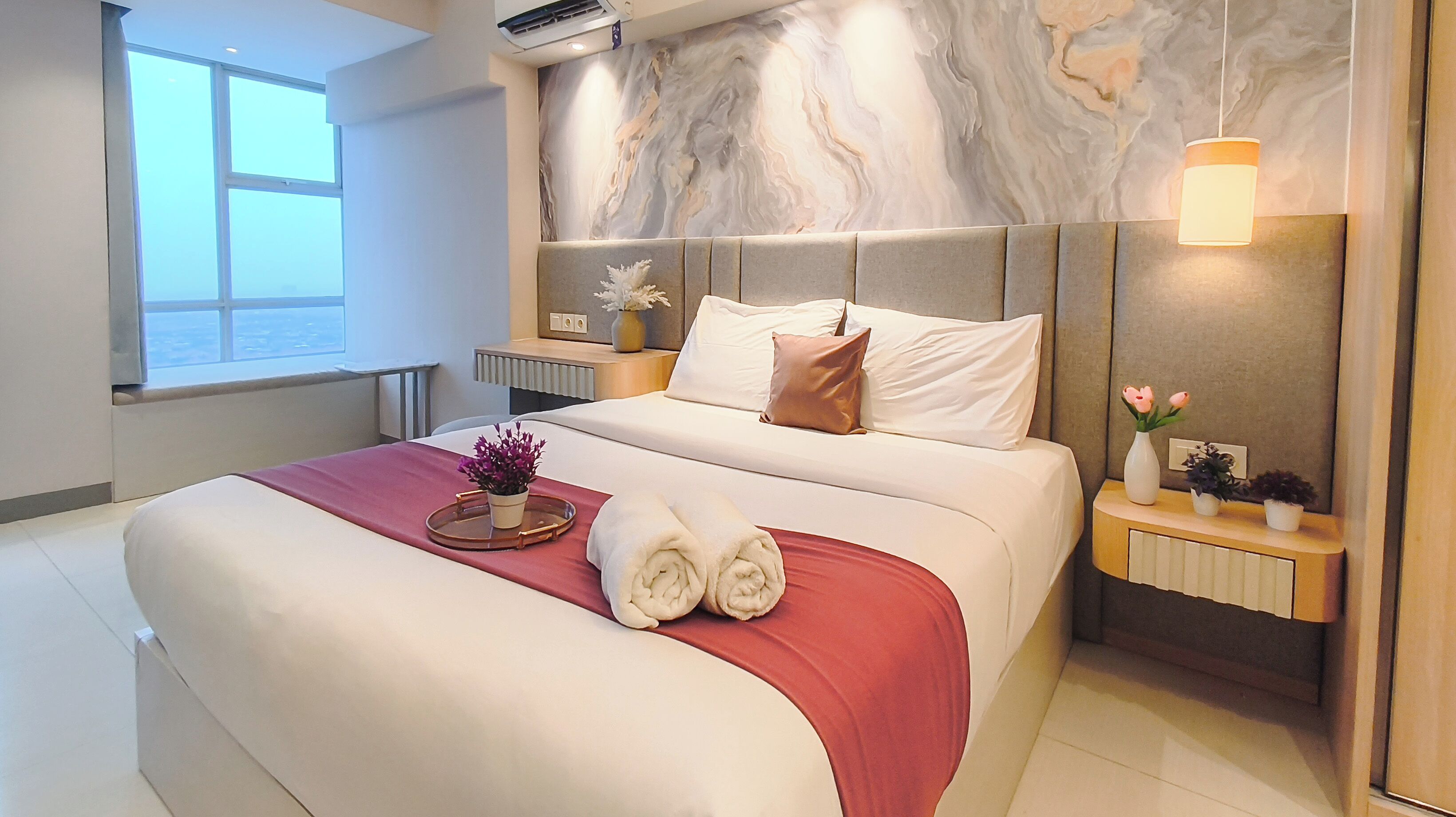 Quarto de hotel moderno com uma cama grande, parede de mármore, janela e mesa de cabeceira com abajur.