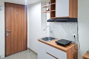 Uma cozinha compacta com porta de madeira, armários brancos, pia de aço inoxidável e exaustor preto.