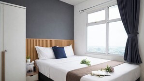 Quarto com cama, janela com cortinas, mesa de cabeceira com planta e vista para a cidade.