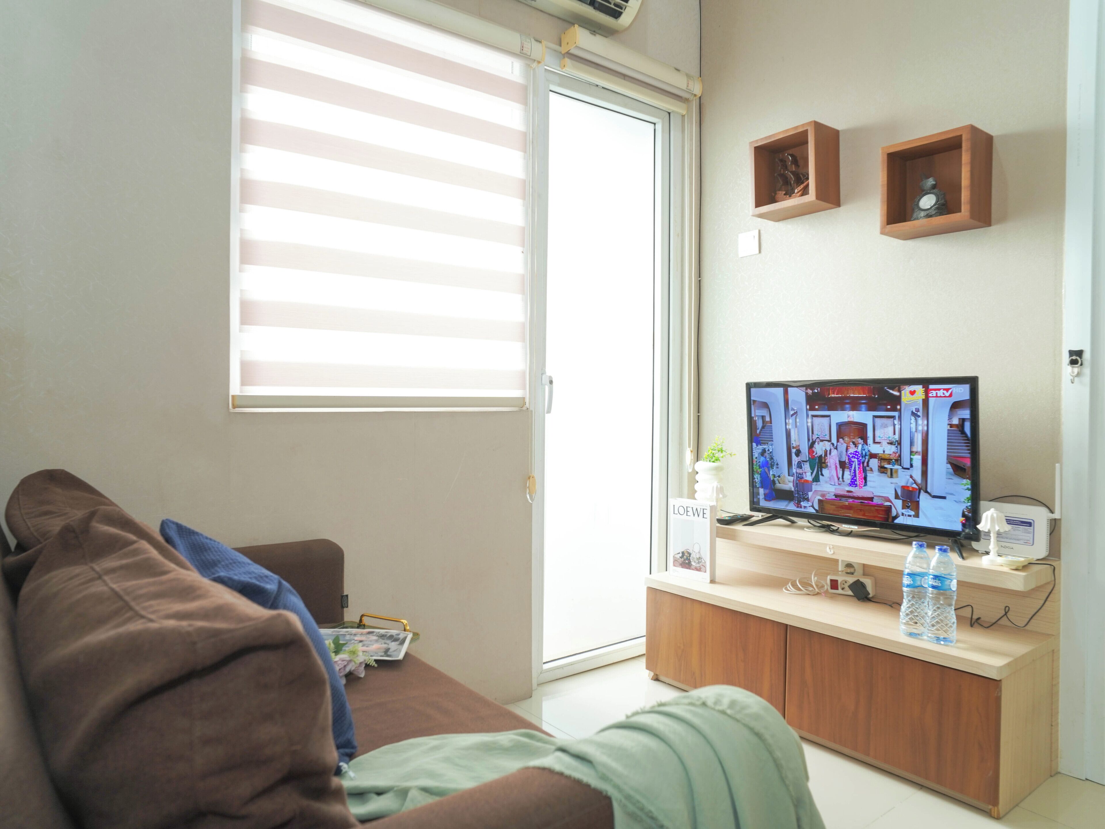Uma sala de estar com sofá, televisão, armário de madeira e janela com persianas.